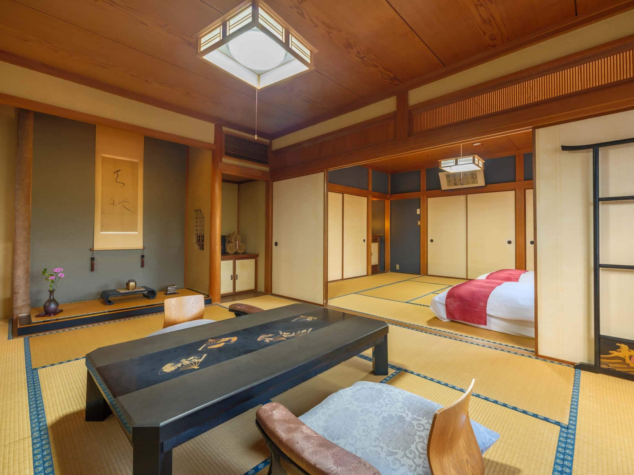 Quarto japonês tradicional com tatames, uma mesa baixa, uma cama com cobertor vermelho e portas deslizantes.