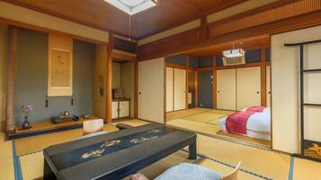 Quarto japonês tradicional com tatames, uma mesa baixa, uma cama com cobertor vermelho e portas deslizantes.