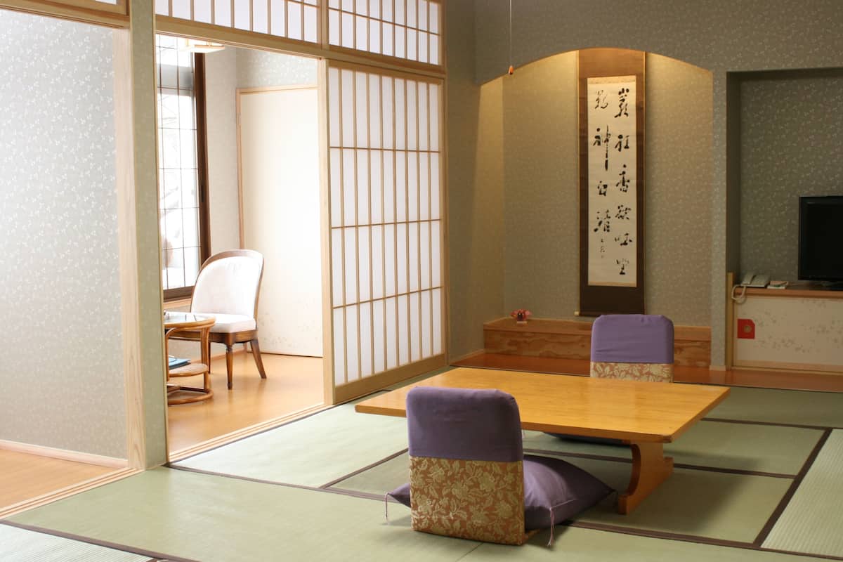 Um quarto japonês tradicional com tatames, uma mesa de madeira baixa, duas cadeiras, um painel deslizante shoji e um rolo de caligrafia na parede.