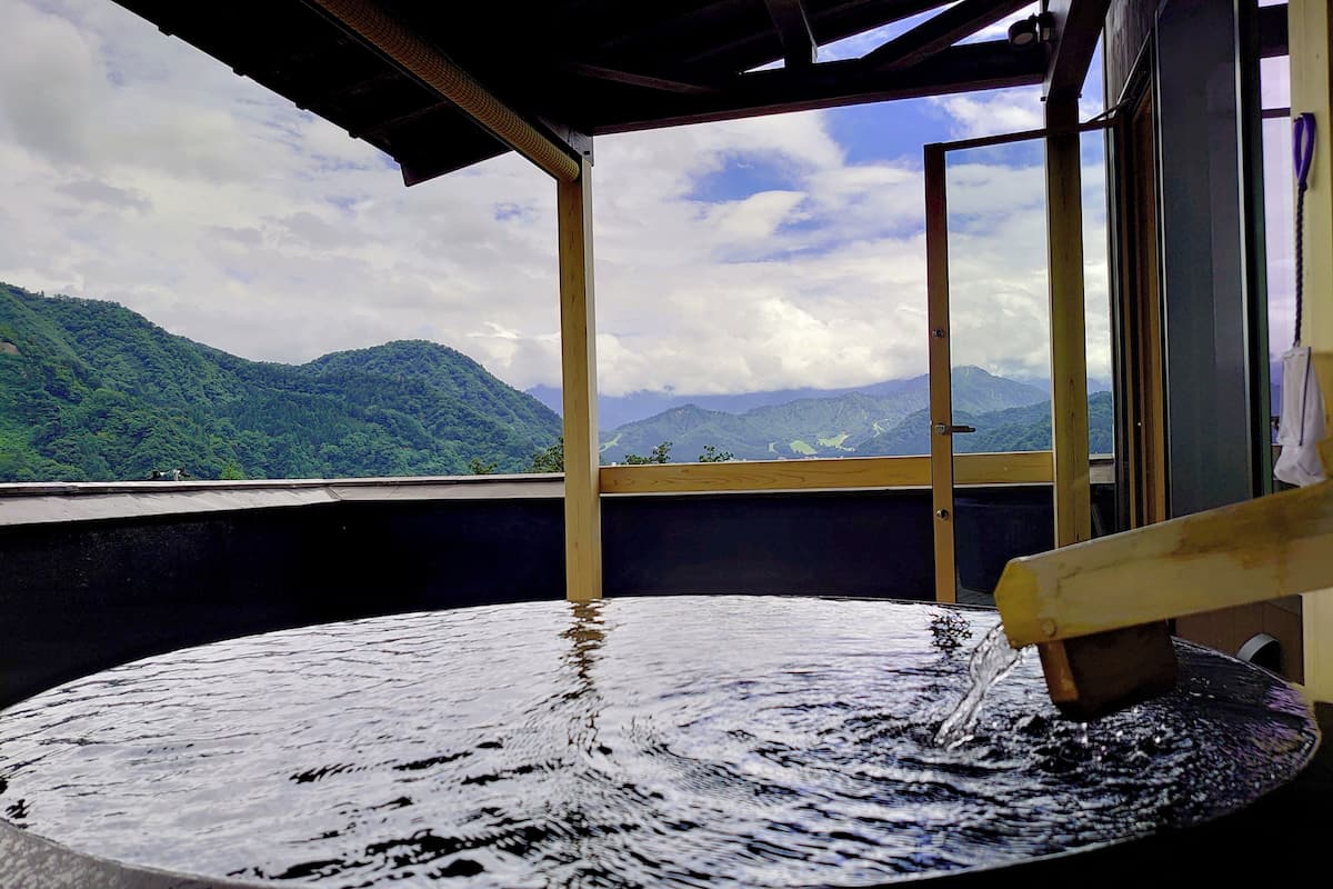 Uma nascente quente com um banco de madeira, vista para montanhas e uma porta entreaberta.