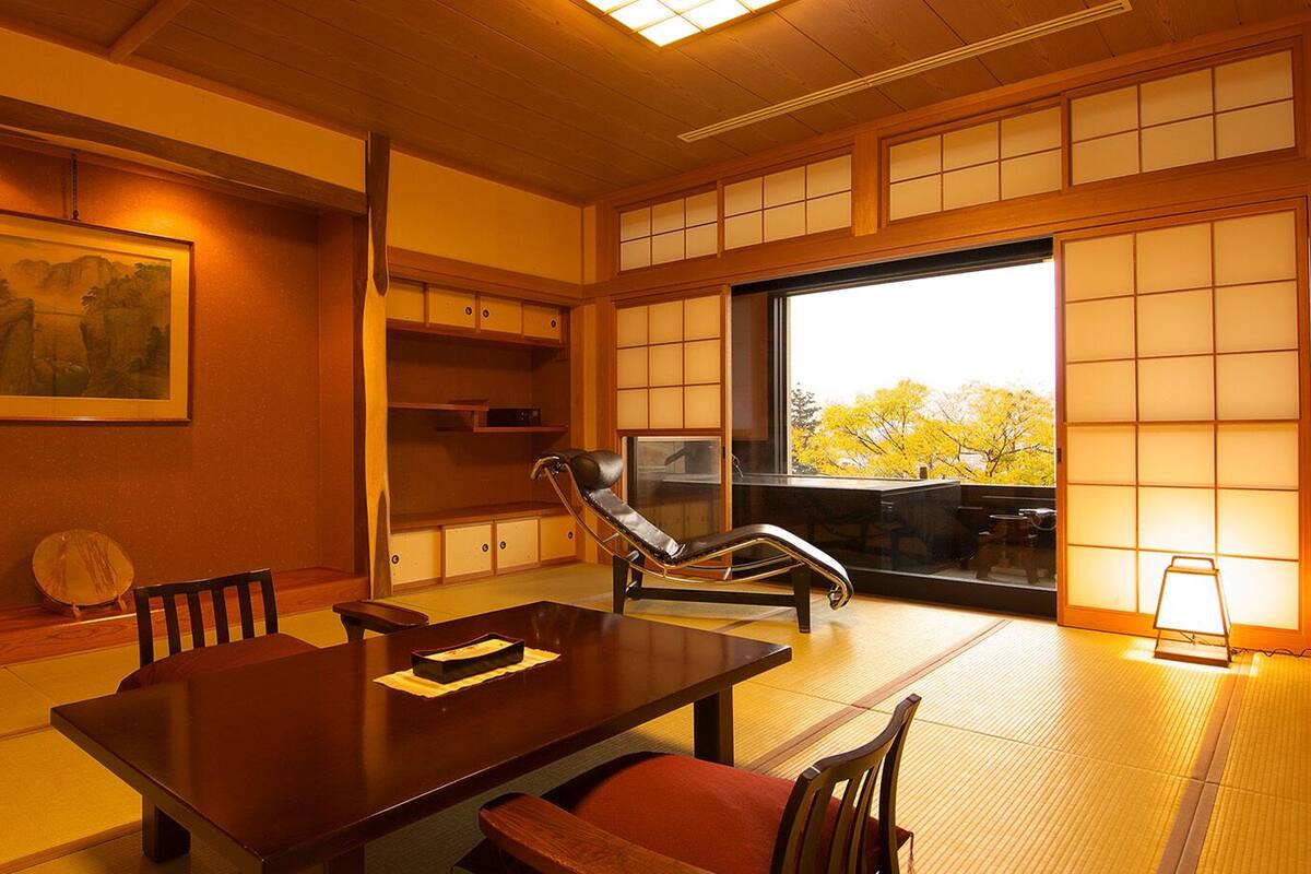 Um quarto japonês tradicional com tatame, uma mesa baixa, uma cadeira estofada, uma porta deslizante e um quadro na parede.