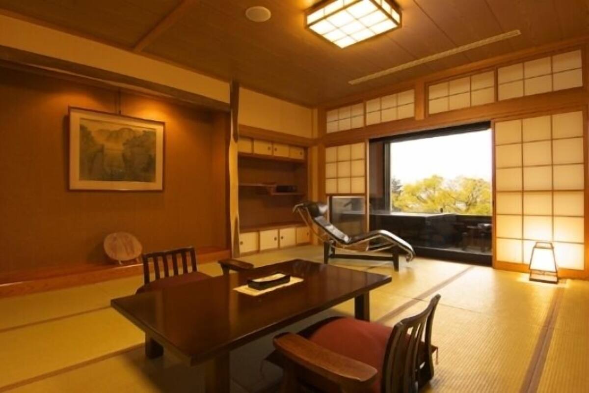 Um espaço com tatames, uma mesa baixa, cadeiras, uma porta de correr e um quadro na parede.
