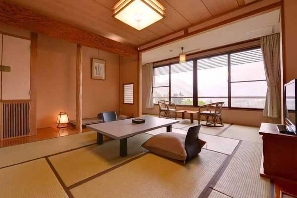 Um quarto em estilo japonês tradicional, com tatames, uma mesa baixa, cadeiras e uma grande janela com vista.