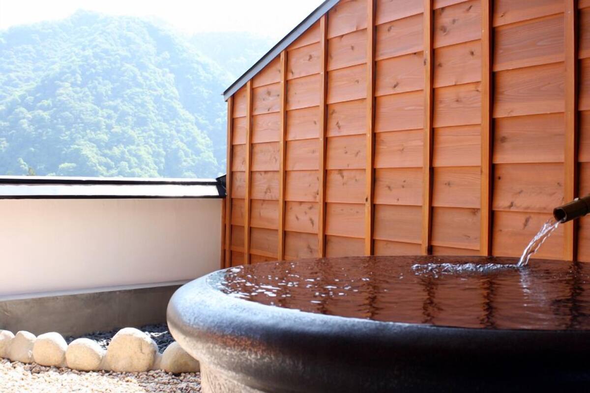 Uma nascente quente com água corrente, cercada por um muro de madeira e vista para uma colina arborizada.