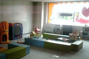 Espaço infantil com estruturas coloridas e uma grande janela com vista para um edifício.