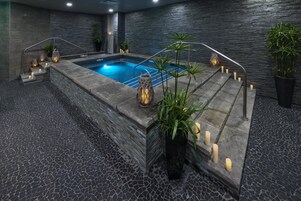 Uma área interna de piscina moderna com parede de pedra, plataforma flutuante e escadaria que dá para a piscina.