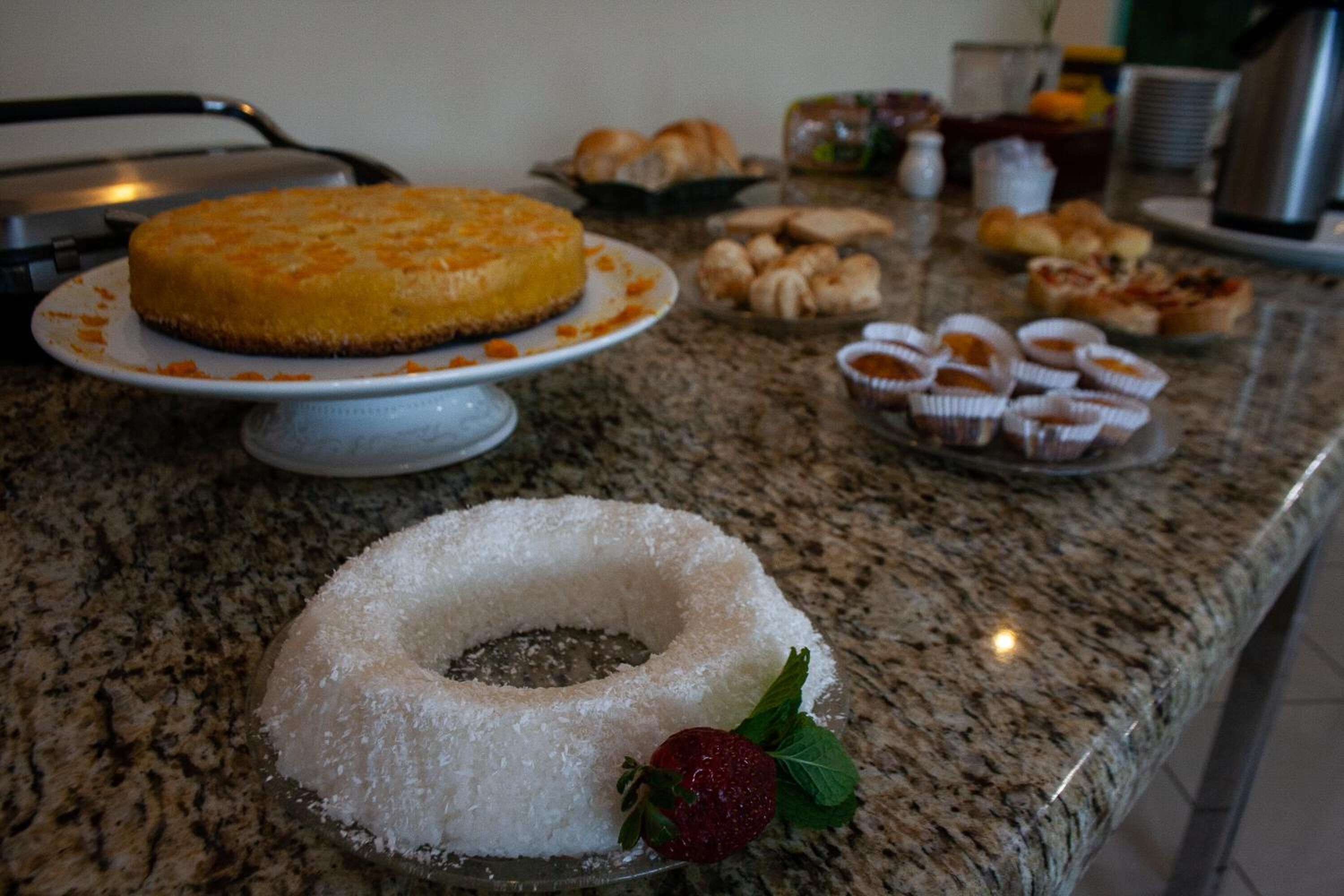 Uma bancada de cozinha com um bolo, cupcakes e doces.