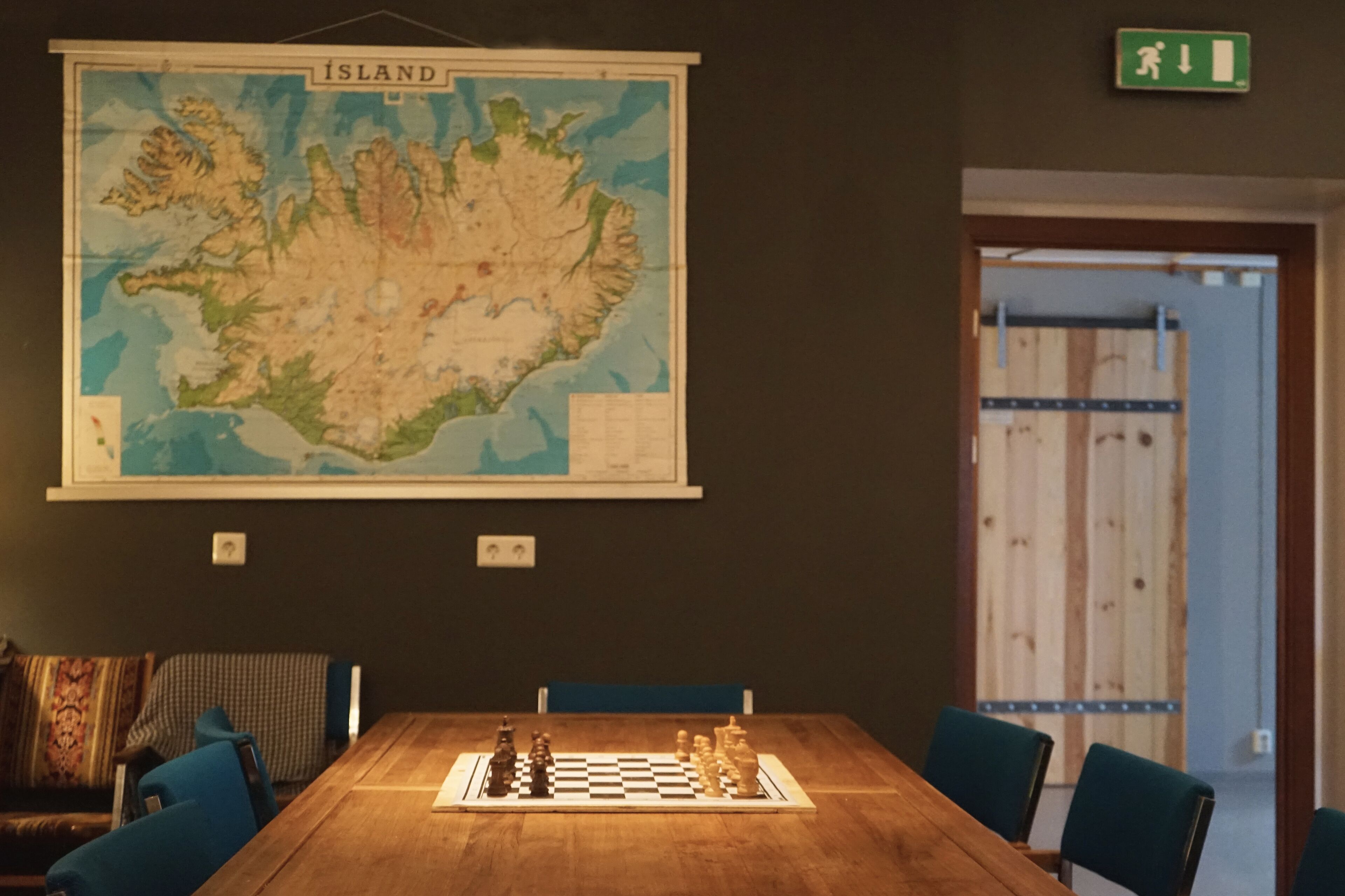 Um quarto com uma mesa de madeira preparada para um jogo, um mapa da Islândia na parede e uma porta com painel de madeira.