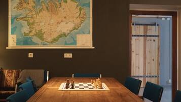 Um quarto com uma mesa de madeira preparada para um jogo, um mapa da Islândia na parede e uma porta com painel de madeira.