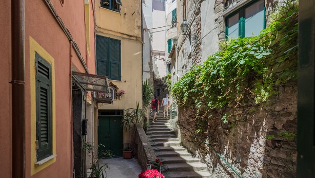 Rua estreita ladeada por edifícios com paredes de pedra e persianas verdes.