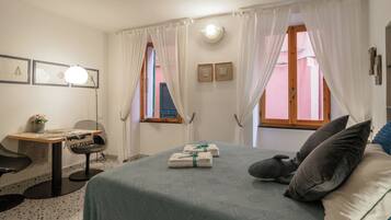 Quarto com cama, almofadas, escrivaninha com cadeira, luminária e cortinas.