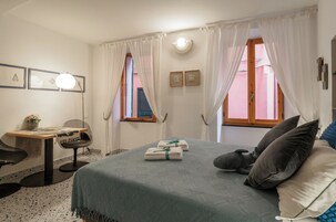 Quarto com cama, almofadas, escrivaninha com cadeira, luminária e cortinas.