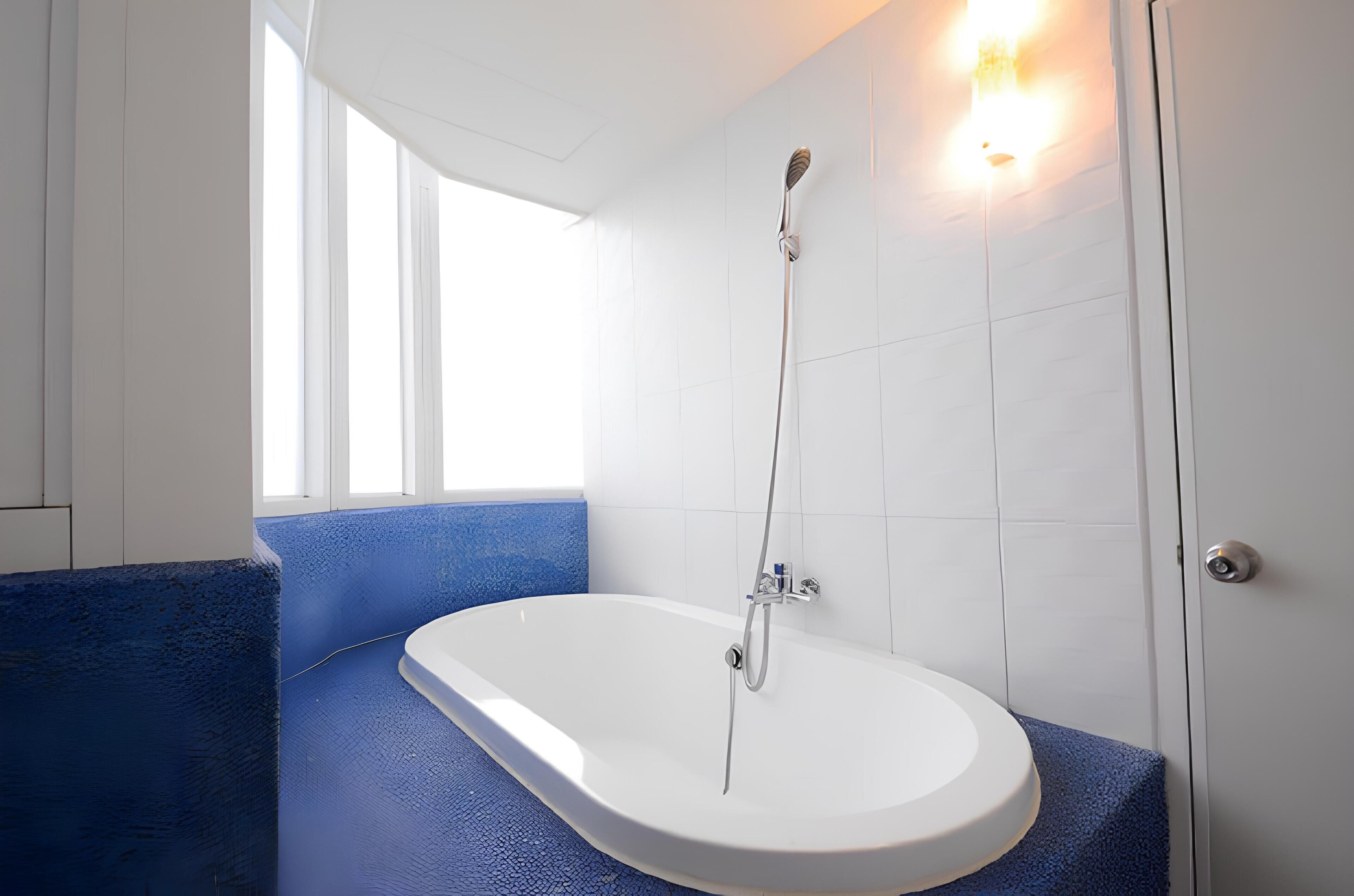 Casa de banho moderna com banheira branca, chuveiro e janela que oferece luz natural.