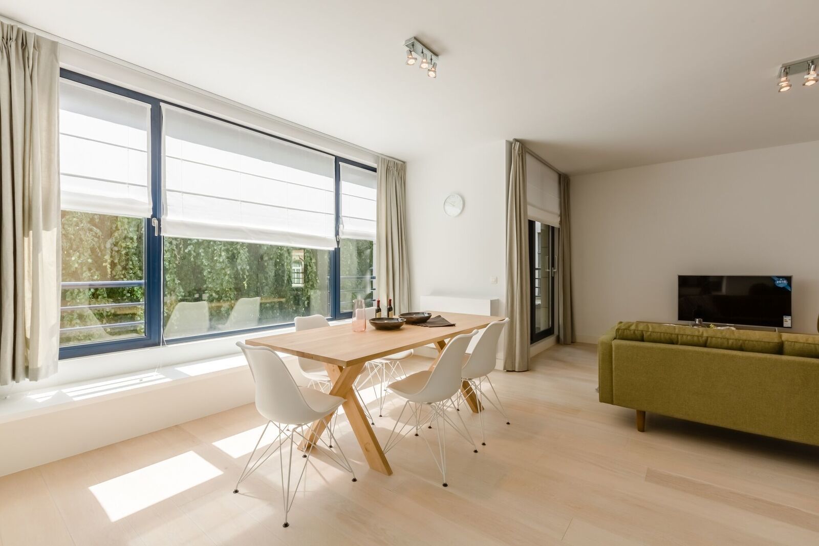 Uma sala de estar moderna com área de jantar, janelas amplas e um sofá verde.