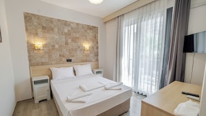 Quarto de hotel com uma cama grande, duas mesas de cabeceira, um aparador de madeira, uma televisão e uma parede com padrão de pedra.