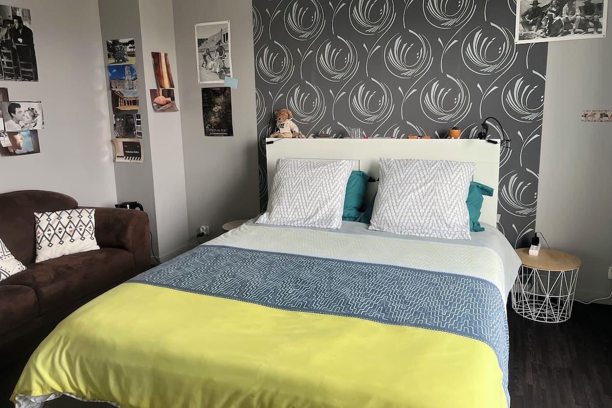 Quarto com cama, poltrona marrom e mesa de cabeceira pequena.