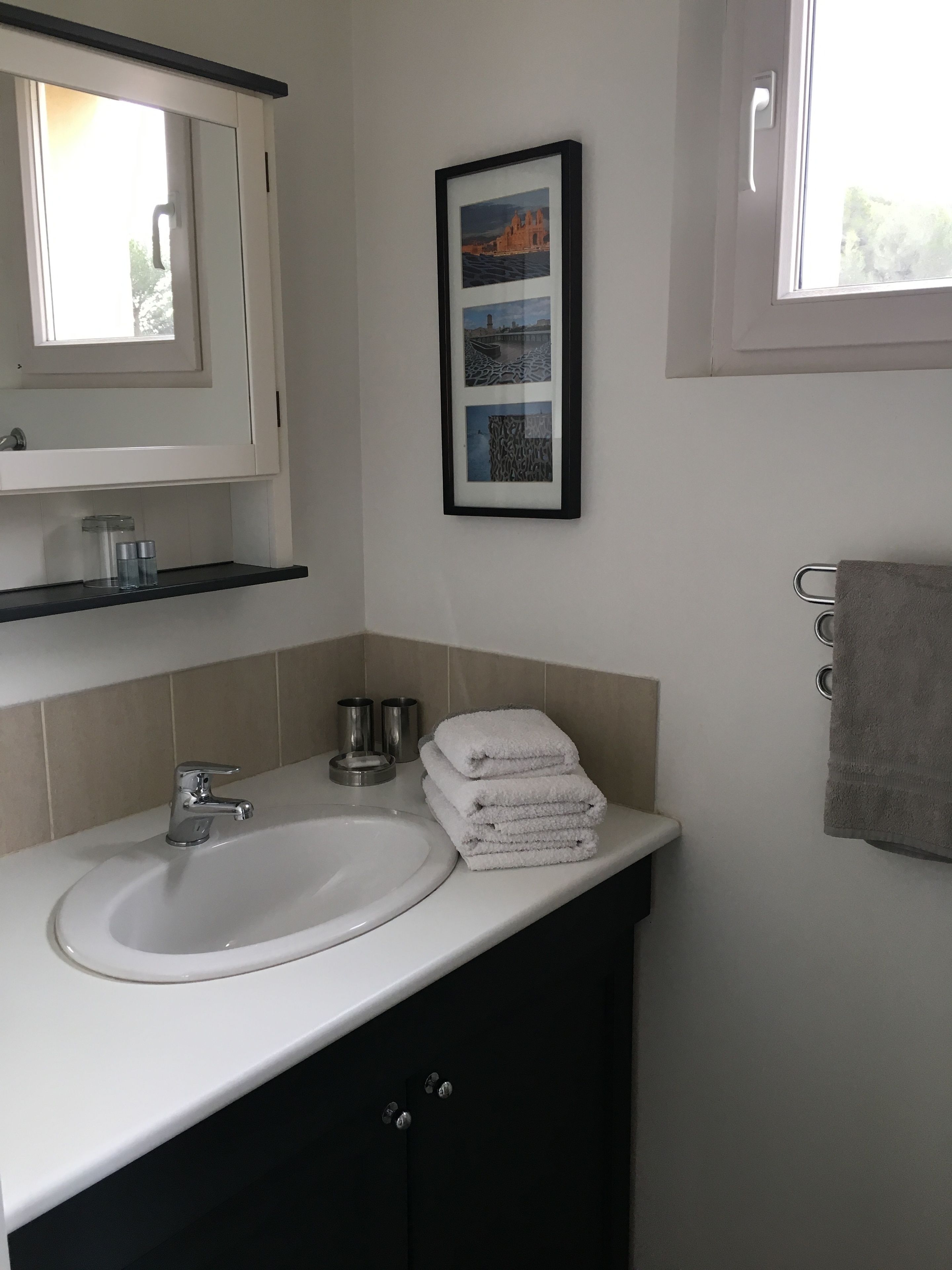 Casa de banho com uma pia branca, um espelho, um quadro emoldurado e um porta-toalhas.