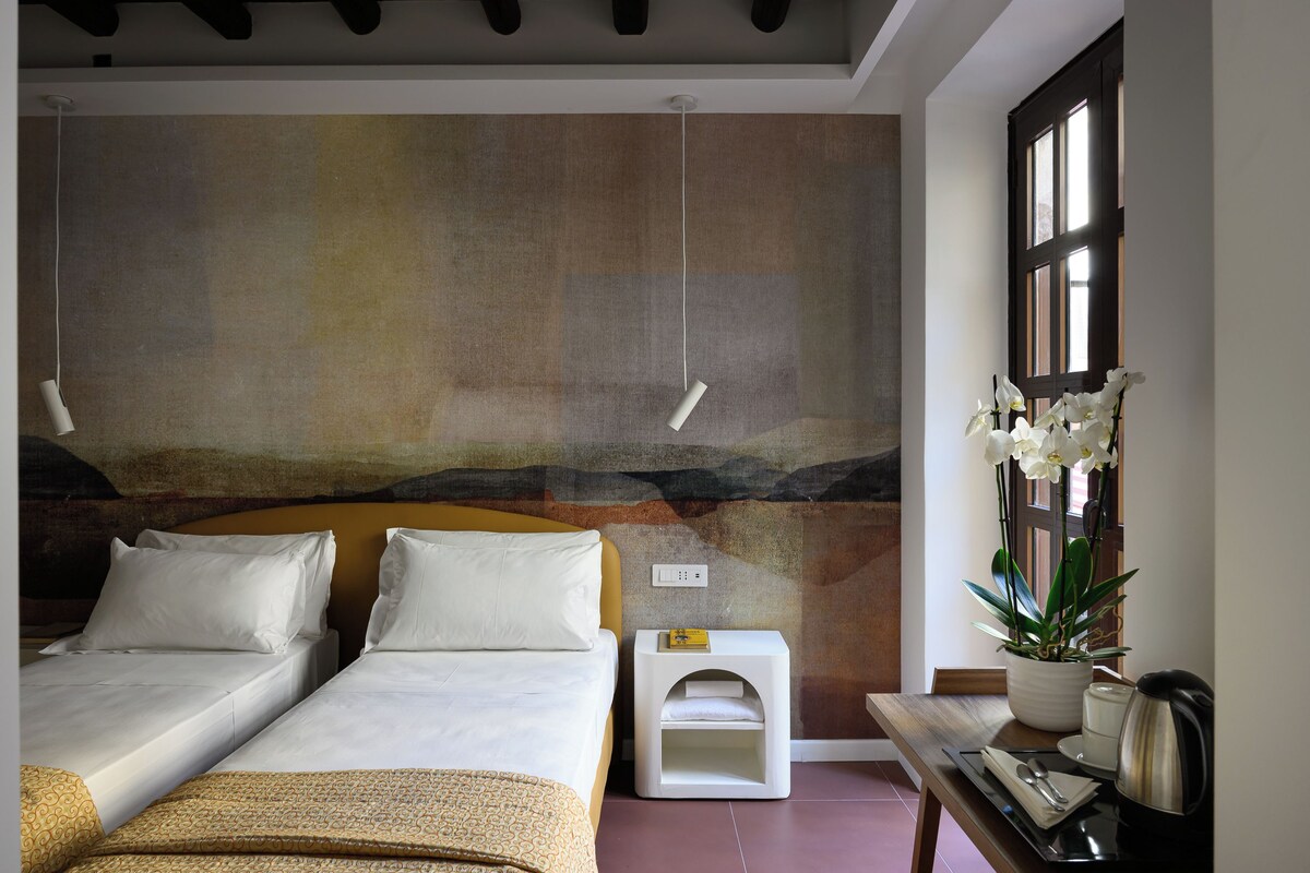 Quarto de hotel com cama, mesa de cabeceira e janela com cortinas.