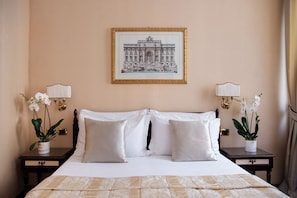 Quarto de hotel com uma cama grande, duas mesas de cabeceira, um quadro na parede e duas orquídeas em vasos.
