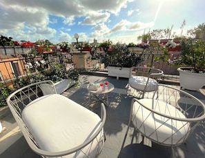 Terraço no telhado com área de estar ao ar livre, plantas em vasos e céu claro.
