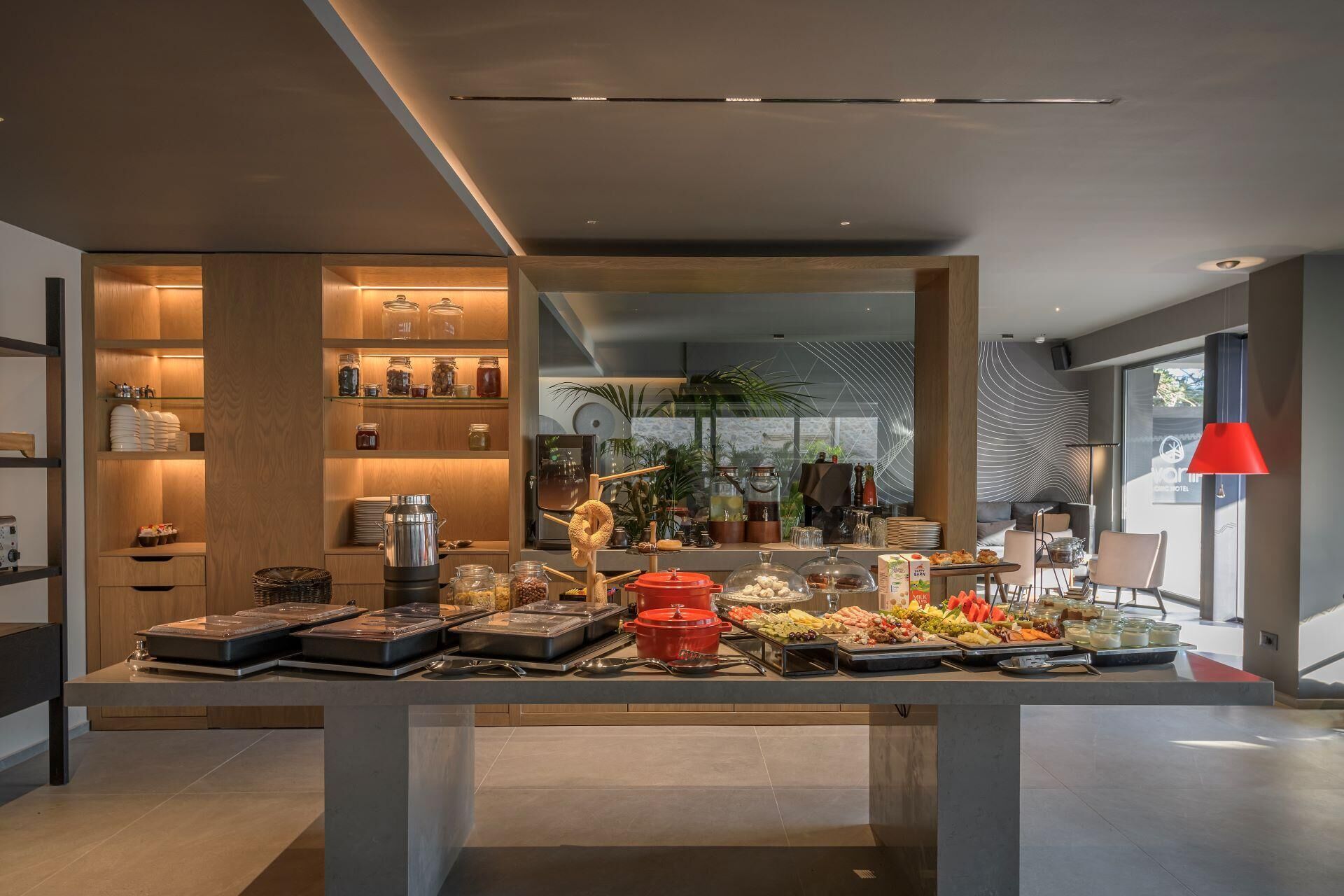 Quarto de hotel moderno com buffet de café da manhã, prateleiras de madeira e vista para o exterior.