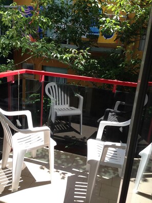 Uma área de pátio com cadeiras de plástico branco e guarda-corpo vermelho.