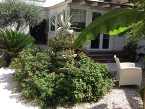 Um jardim com diversas plantas e uma cadeira de vime branca.