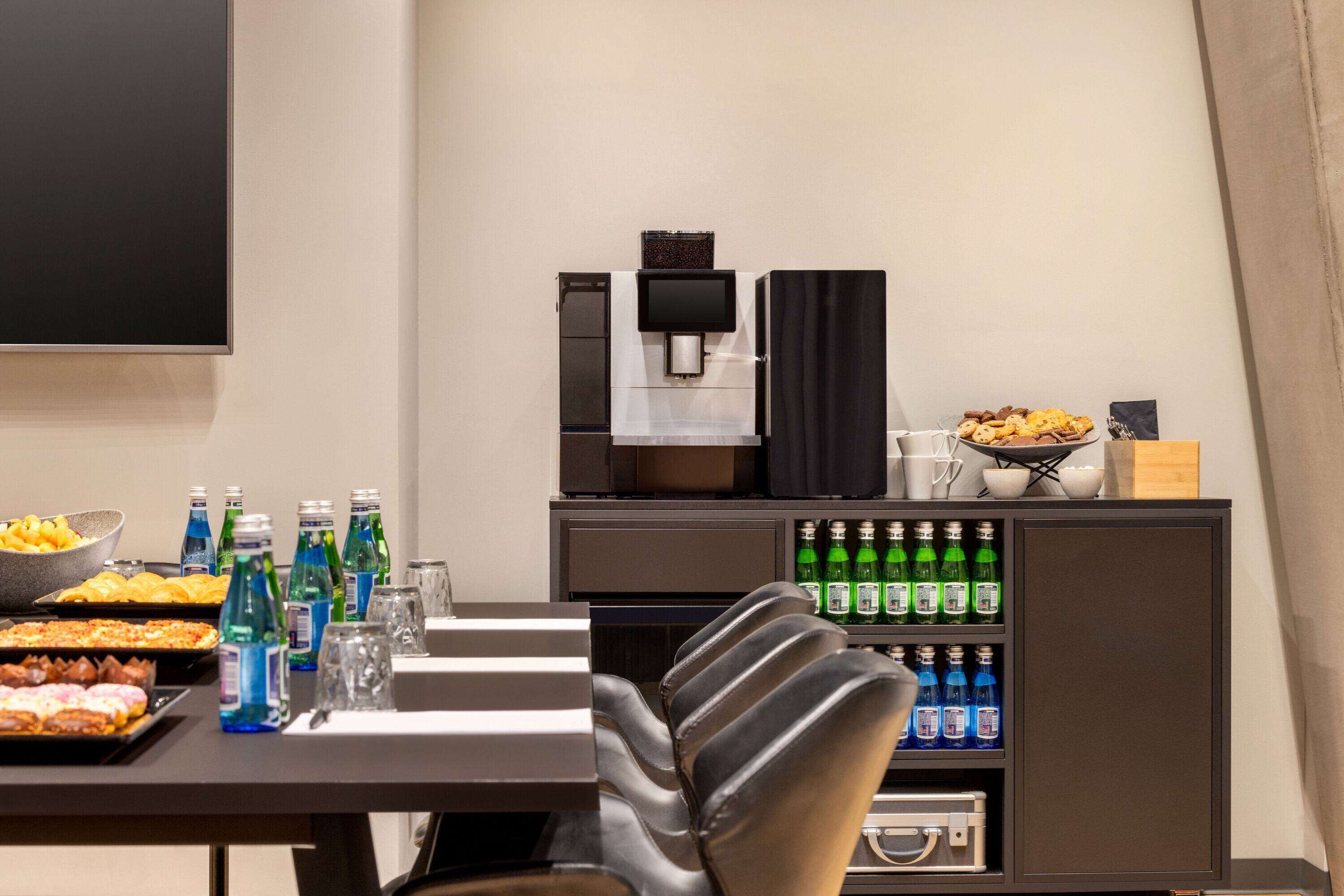Quarto de hotel com uma mesa de jantar posta com comida, bebidas e uma máquina de café.