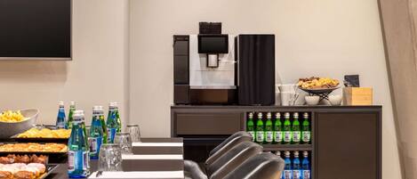 Quarto de hotel com uma mesa de jantar posta com comida, bebidas e uma máquina de café.