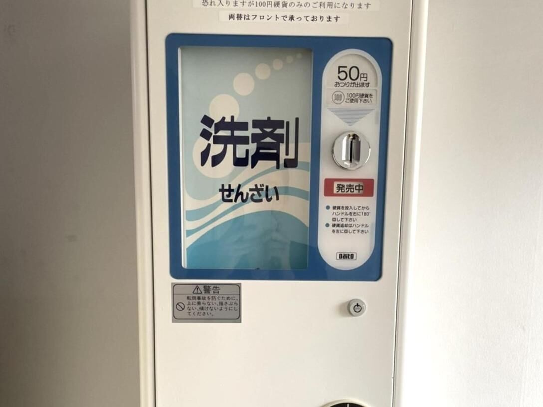 Máquina de vendas automática com texto em japonês, entrada para moeda de 50 ienes e um botão com a inscrição '発売中' (em estoque).