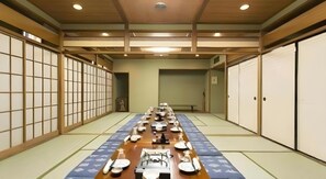 Quarto japonês tradicional com tatames, uma mesa comprida posta para refeição e portas deslizantes em ambos os lados.