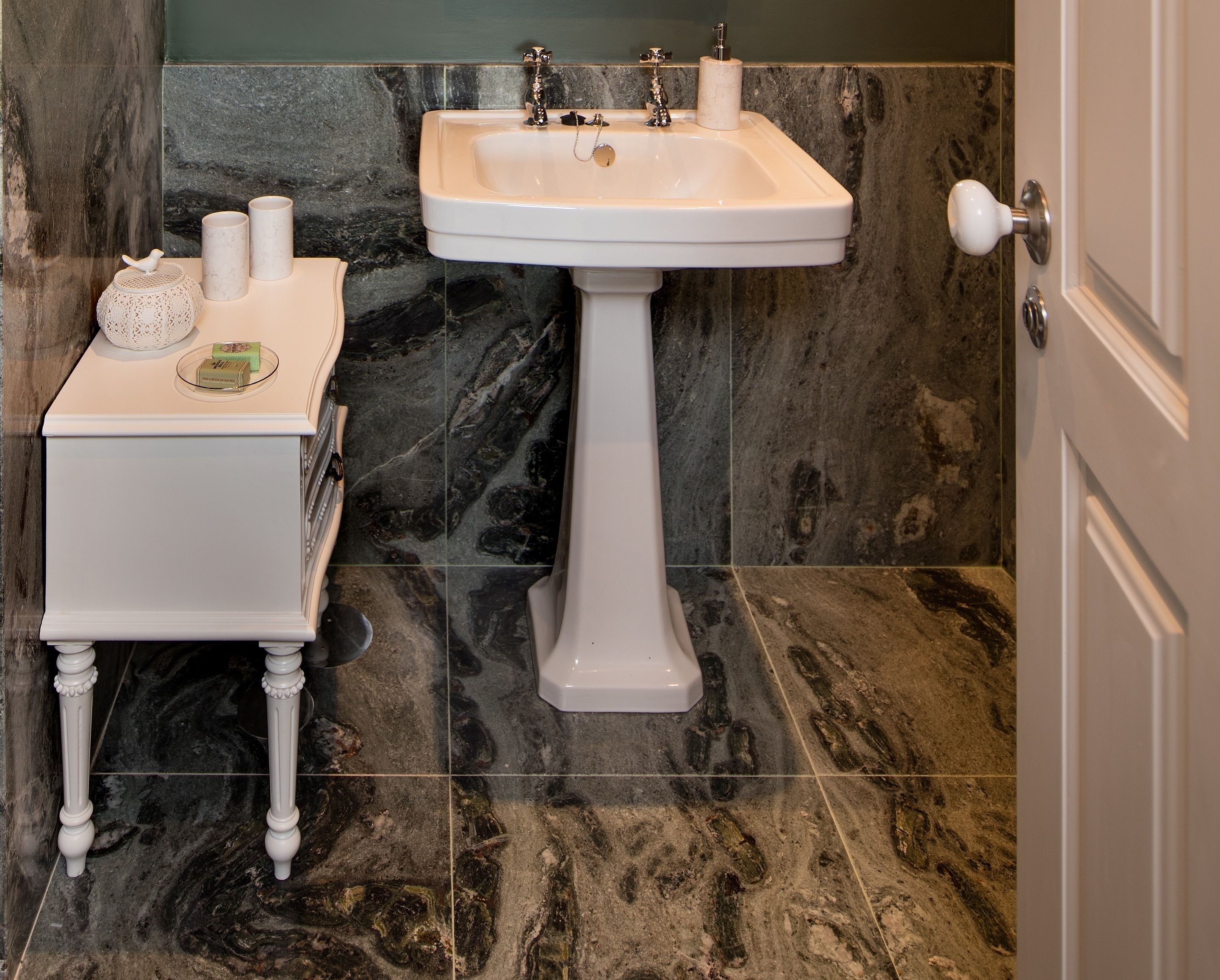 Casa de banho com lavatório pedestal e pequena mesa de toucador, ambos em branco.