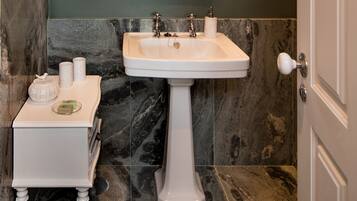 Casa de banho com lavatório pedestal e pequena mesa de toucador, ambos em branco.