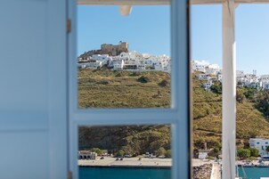 Uma cidade costeira com edifícios brancos, uma construção imponente no alto de uma colina e um porto com barcos.