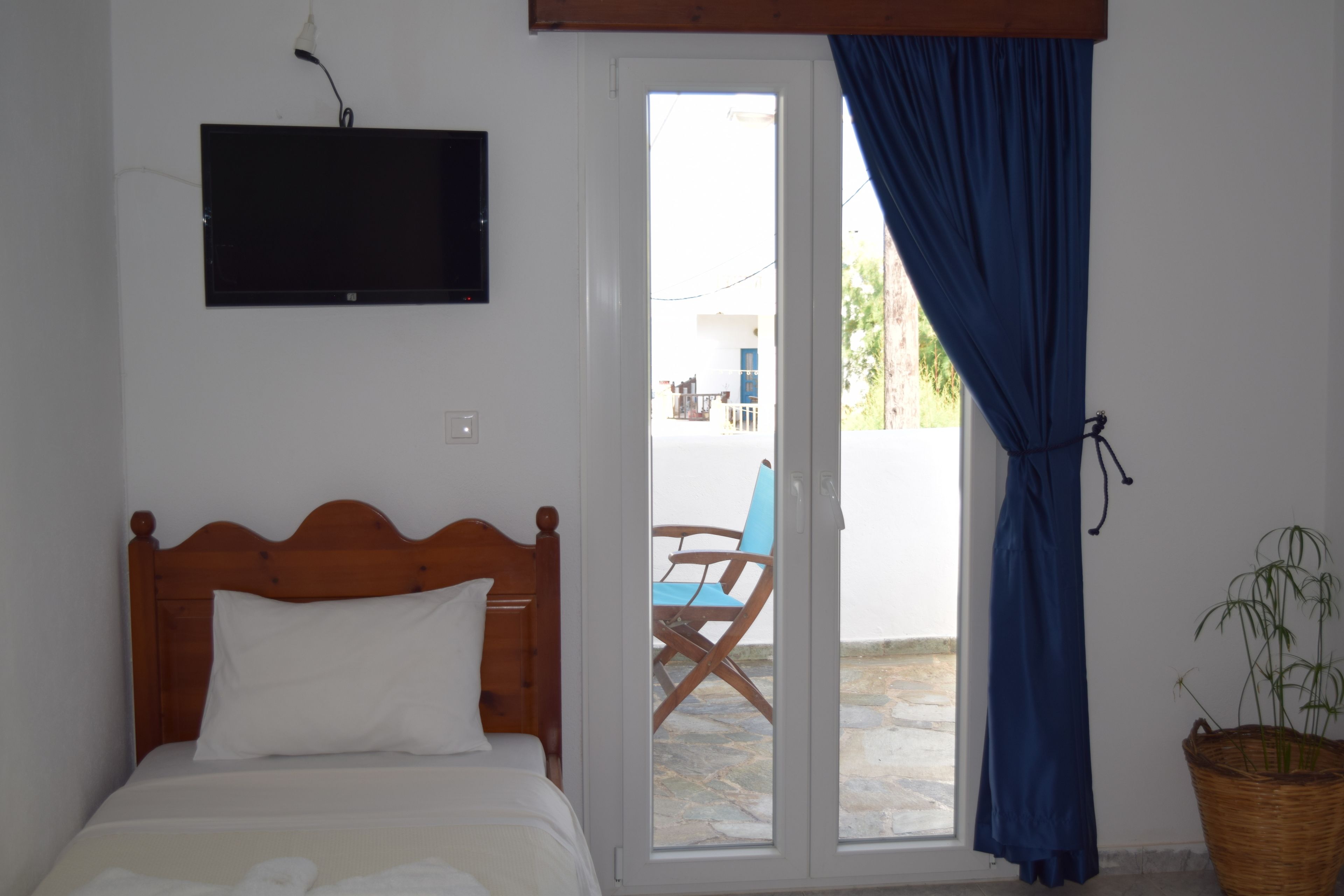 Quarto com cama de madeira, televisão na parede, porta de vidro deslizante e cesto de vime.