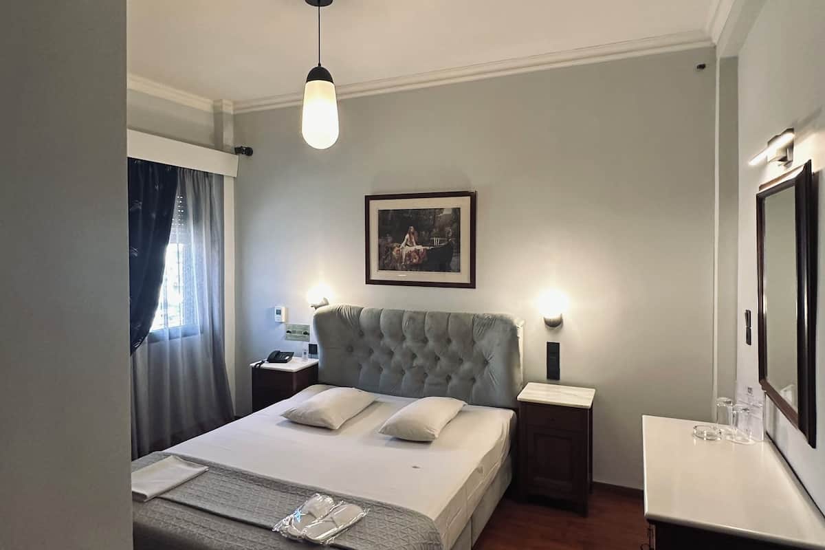Quarto de hotel bem arrumado, com uma cama grande, mesas de cabeceira, uma escrivaninha e um espelho.