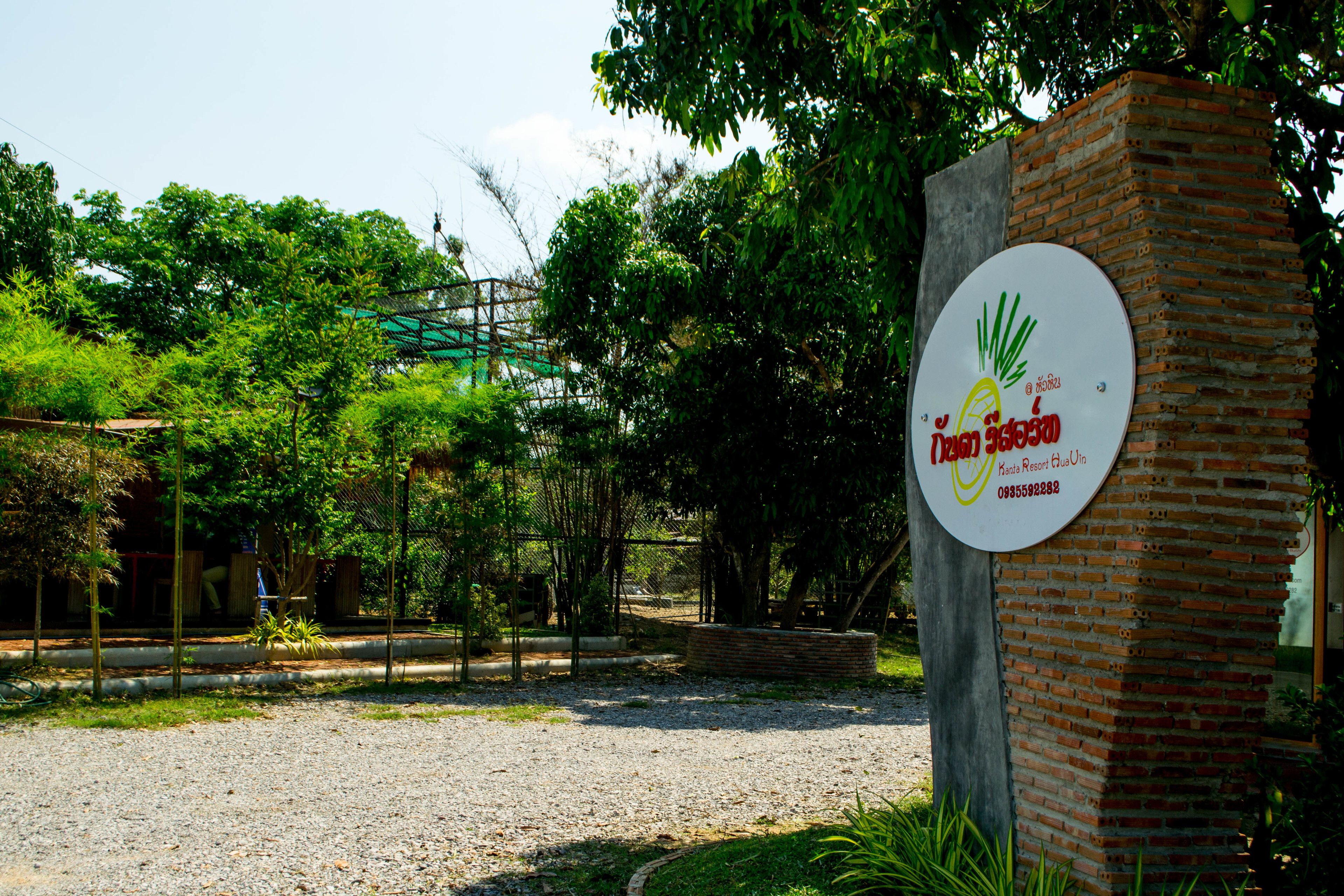 Placa de hotel com logotipo e nome, em meio à vegetação e um caminho de cascalho.