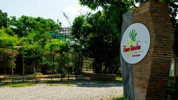 Placa de hotel com logotipo e nome, em meio à vegetação e um caminho de cascalho.