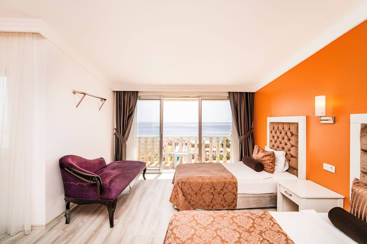 Quarto de hotel com varanda, duas camas, uma cadeira e uma escrivaninha.