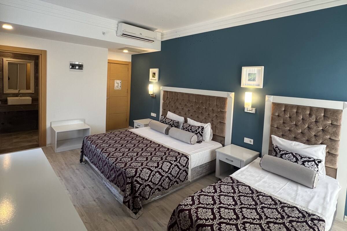 Quarto de hotel com duas camas, uma escrivaninha branca e um guarda-roupa embutido.
