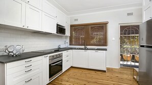 Cozinha moderna com armários brancos, bancada preta, geladeira de aço inoxidável e piso de madeira.