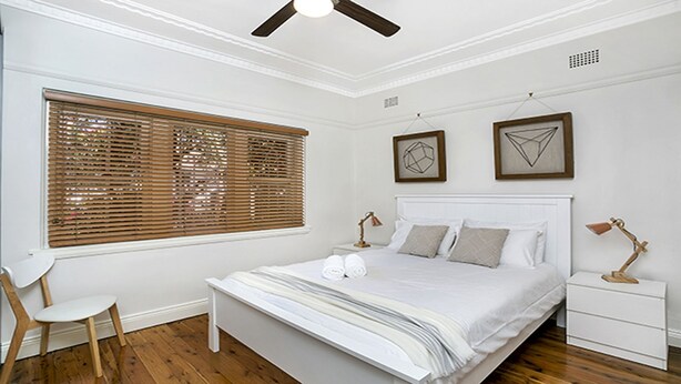 Quarto com cama grande, duas mesas de cabeceira, uma cadeira e um ventilador de teto.