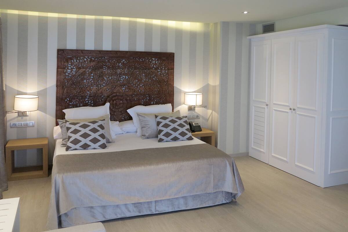 Quarto bem arrumado com uma cama grande, duas mesas de cabeceira com luminárias, um cabeceira decorativa e um guarda-roupa.