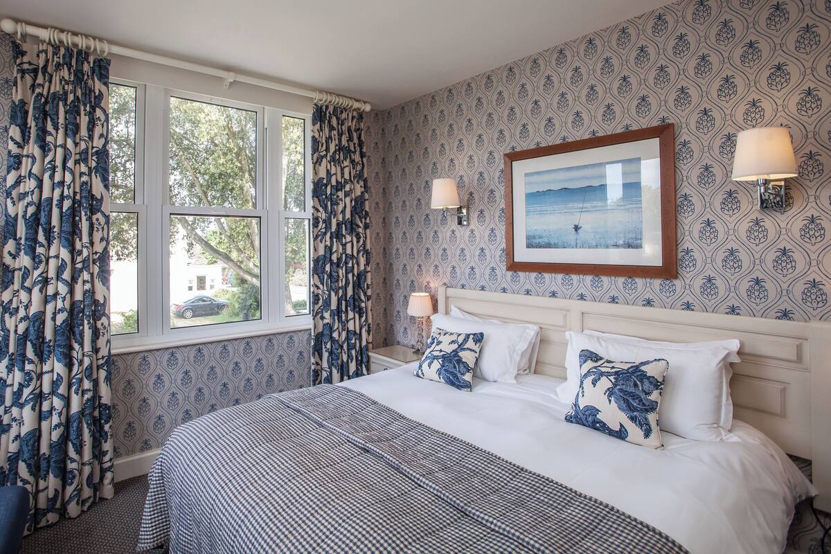Quarto de hotel com cama, duas luminárias de cabeceira, um quadro na parede e uma janela com cortinas.
