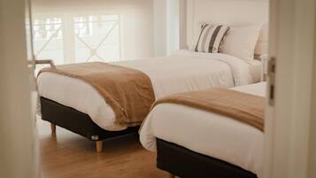 Quarto com duas camas, soalho de madeira e cabeceira branca.