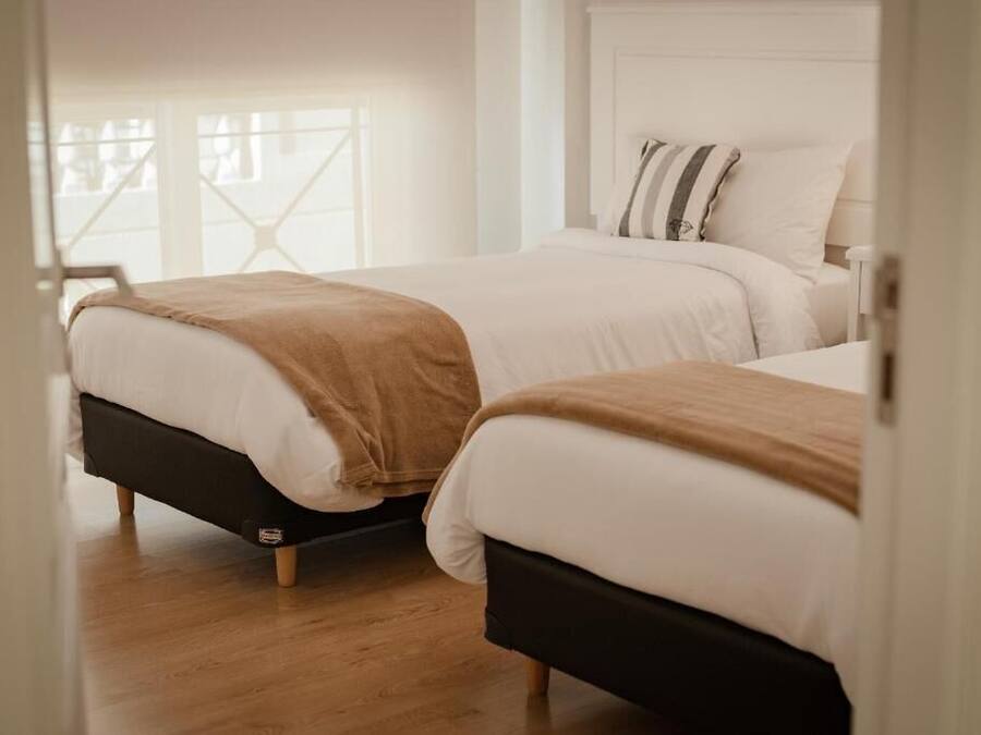 Quarto com duas camas, soalho de madeira e cabeceira branca.