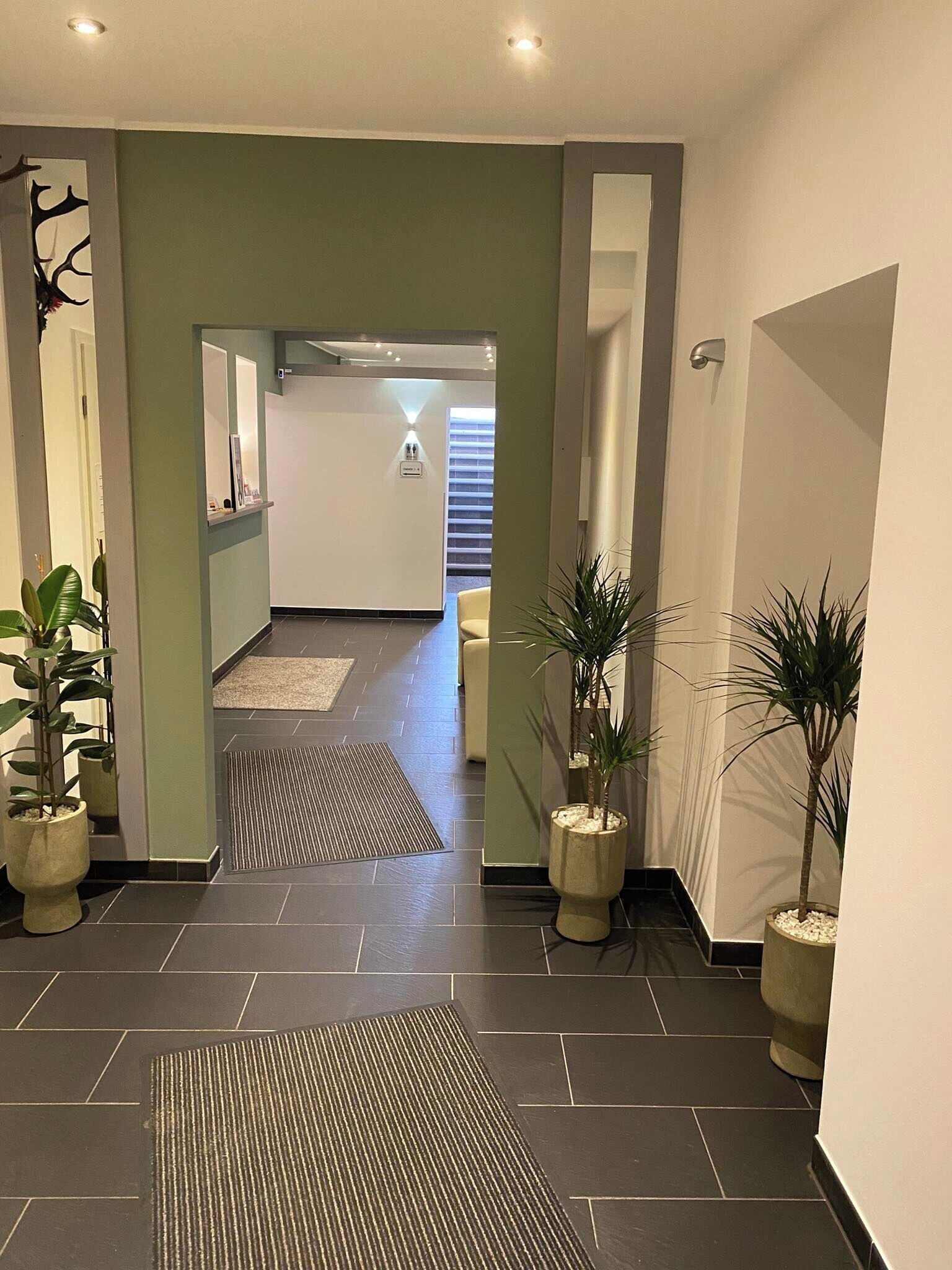 Um corredor com carpete, plantas em vasos e uma porta que dá para um quarto.