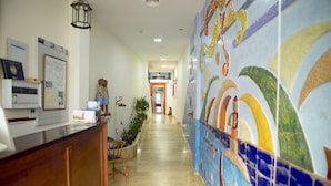 Um saguão de hotel com uma mesa de recepção, um mural e um corredor que dá para o elevador.