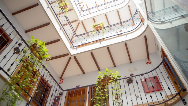 Um átrio com vários níveis, varandas, vigas de madeira e plantas em vasos.