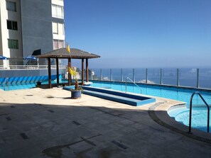 Piscina no terraço com um belvedere, céu azul límpido e vista para o oceano.